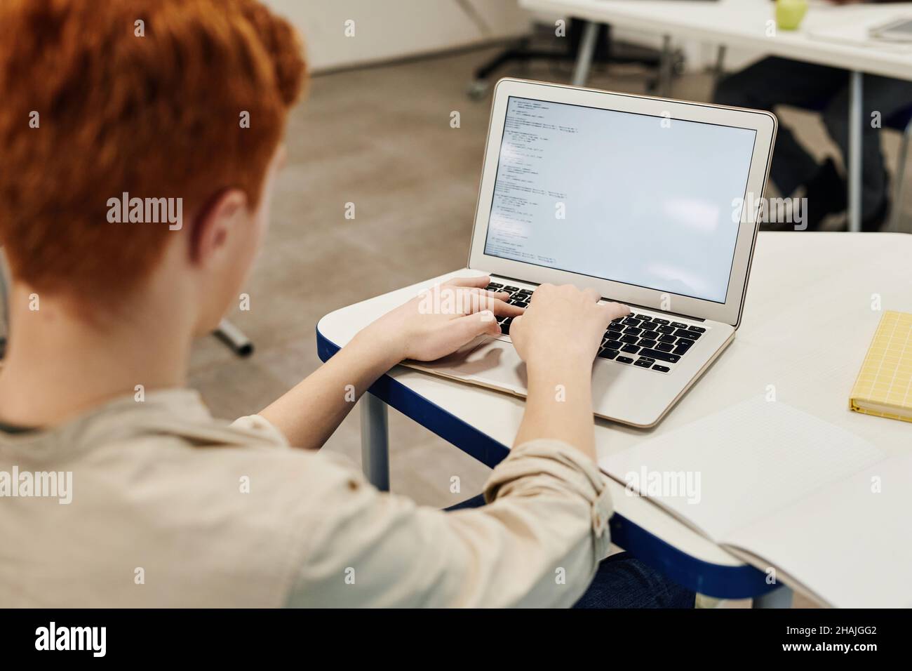 Portrait of red haired teenage boy using laptop while coding in school ...