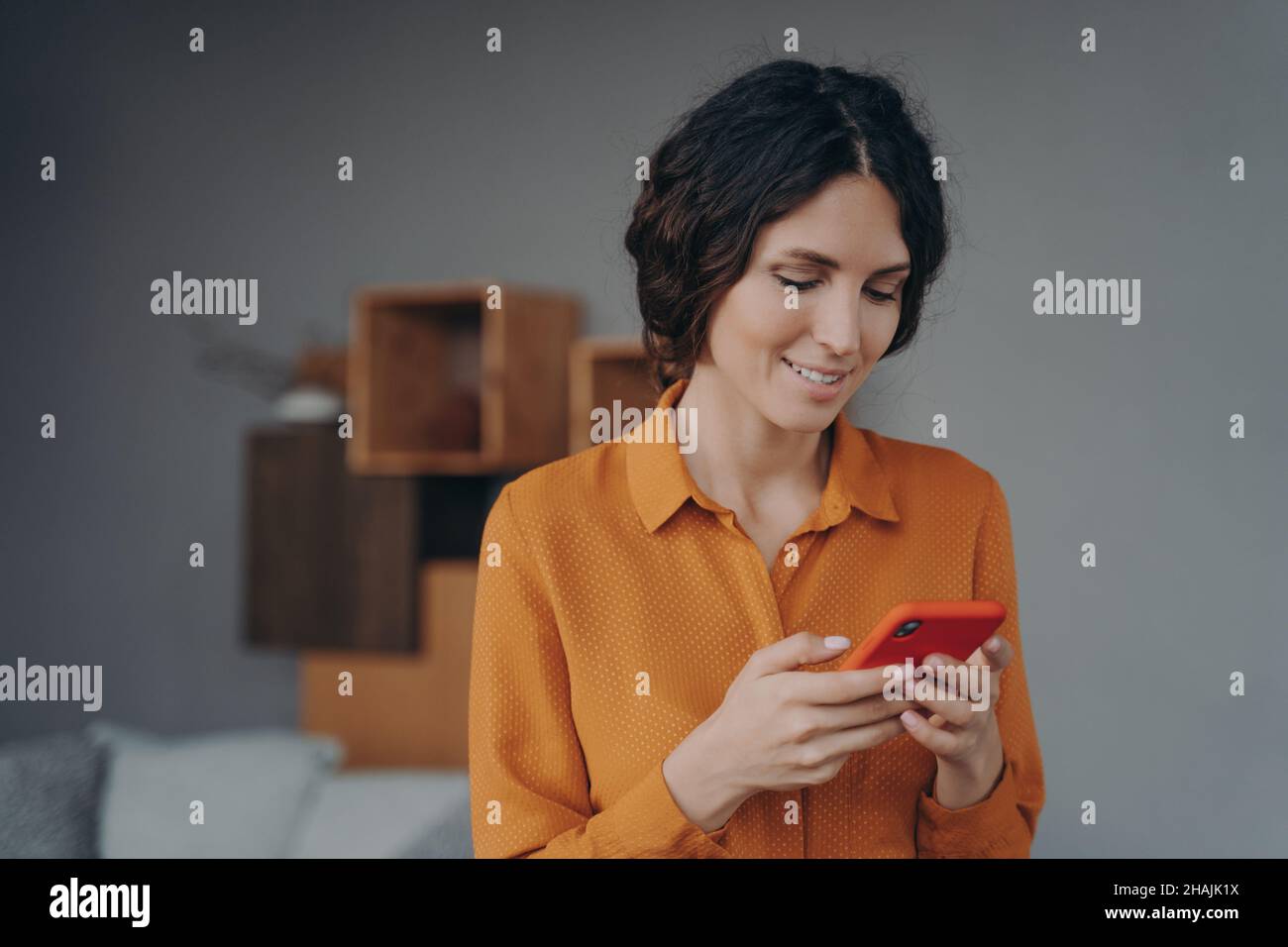 Young smiling hispanic lady holding smartphone, looking at screen with ...