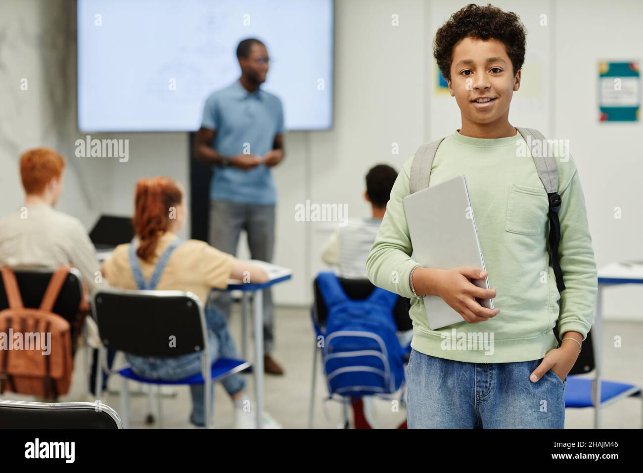 Waist up portrait of smiling teenage boy holding books and looking at ...