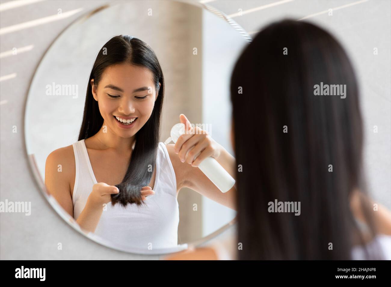 Happy long-haired young asian woman using hair spray Stock Photo - Alamy