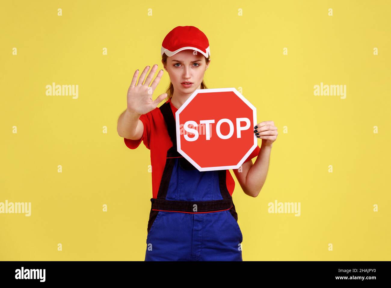 Portrait of worker woman showing stop gesture and holding red stop road ...