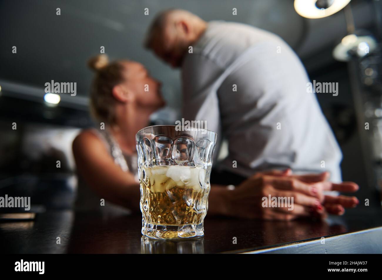 Focus on a glass of alcoholic drink and ice cubes against a blurred ...