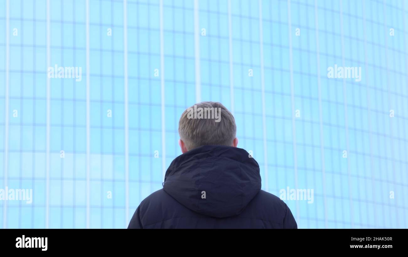 Rear view of man looking at glass building. Media. Man stands and looks ...