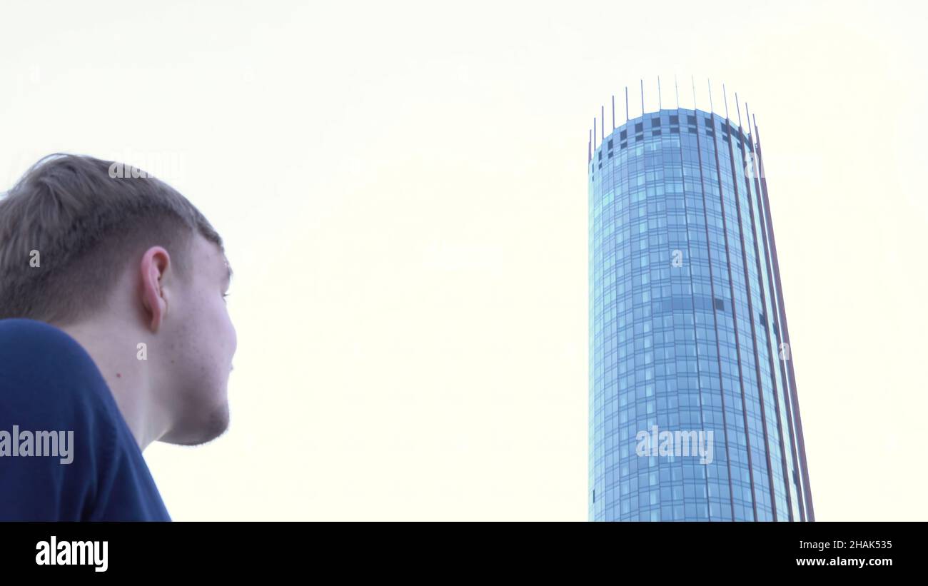 Rear view of man looking at glass building. Media. Man stands and looks ...