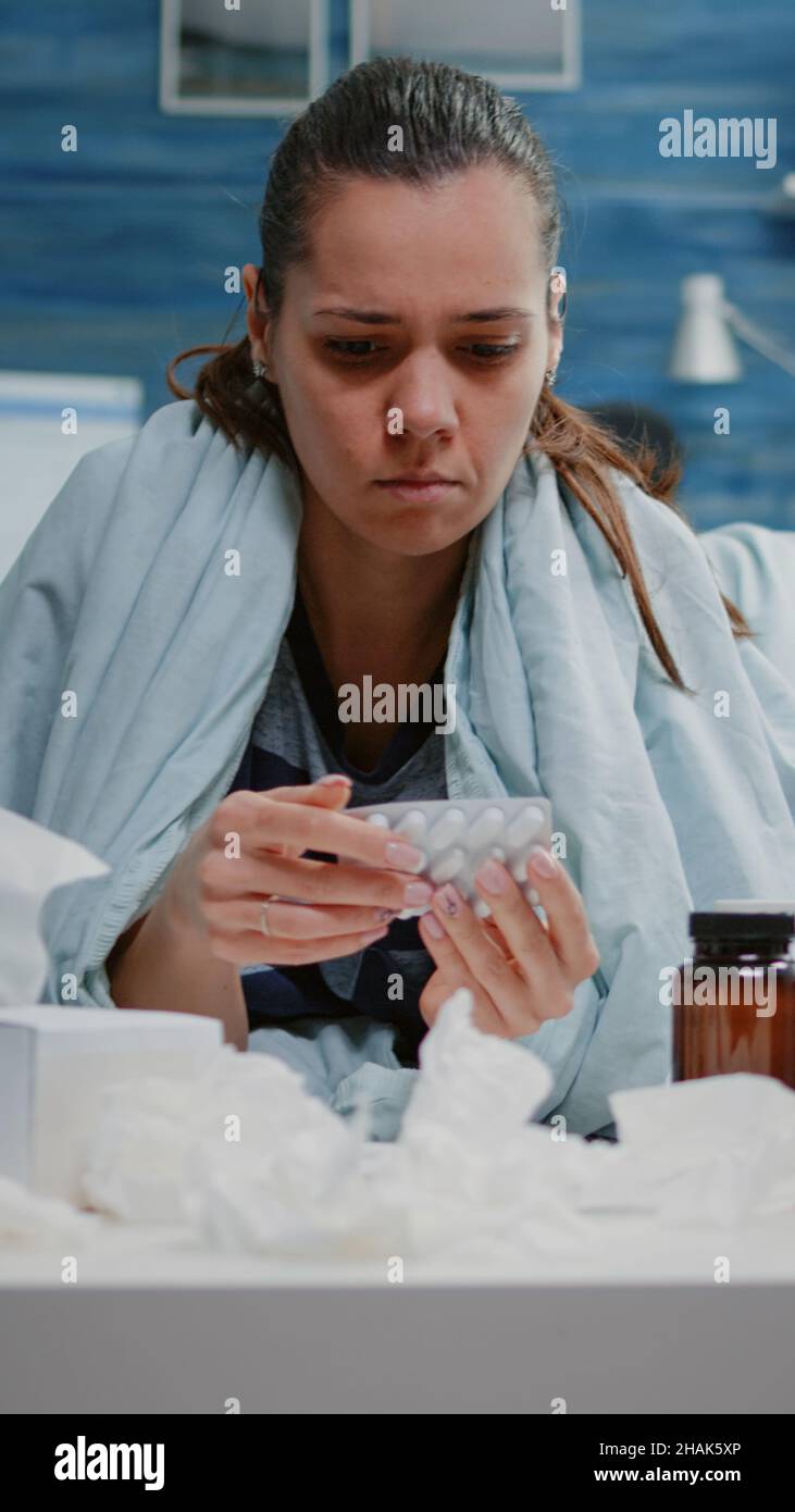 Woman looking at tablets of capsules and jar of pills on table finding ...