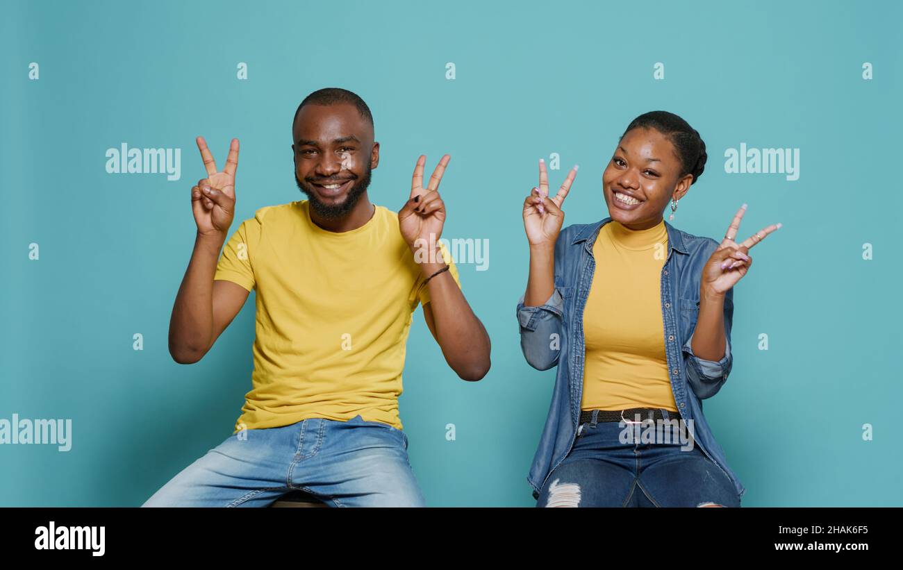 Cheerful couple advertising peace sign with fingers together on camera ...