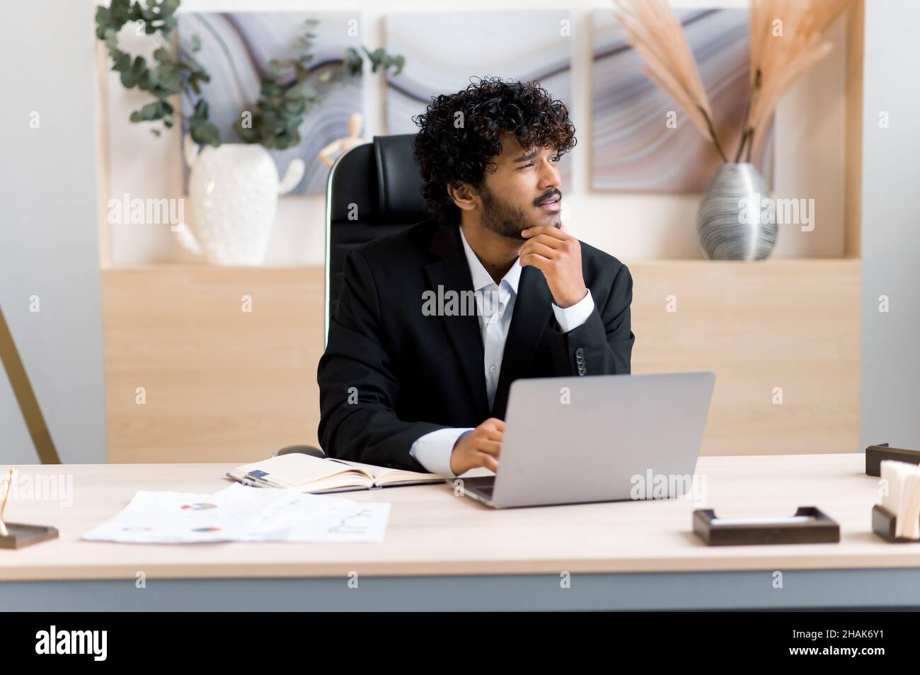 Pensive young successful curly-haired Indian ceo, top manager or ...