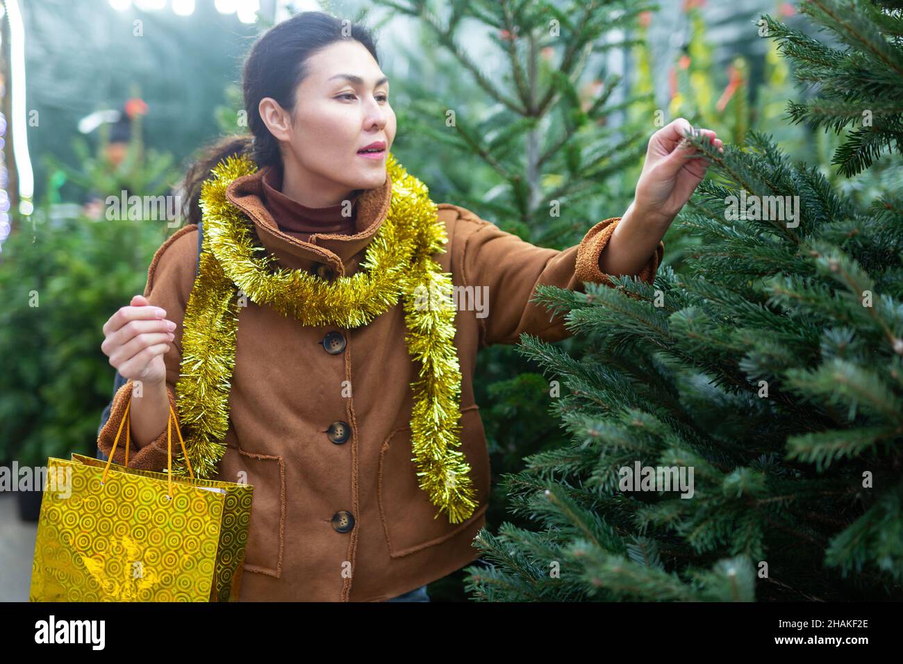 Positive asian woman choosing New Year's tree in christmas street fair ...