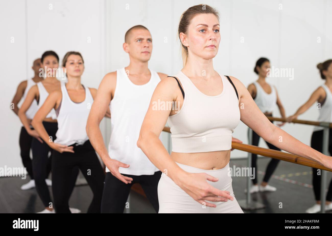 .Group of multiethnic dancers standing with one hand on barre and ...