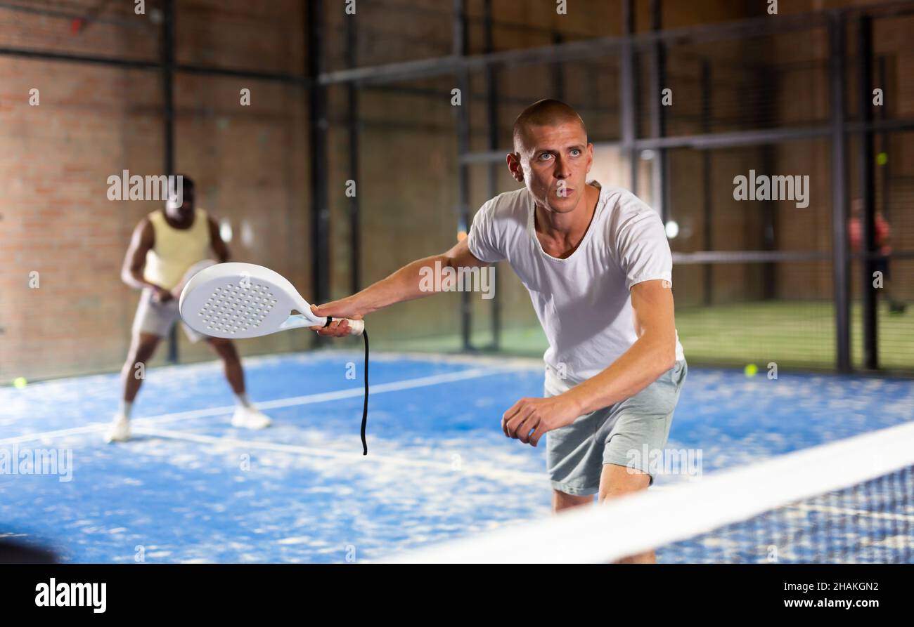 Concentrated man padel player hitting ball with a racket on a hard ...