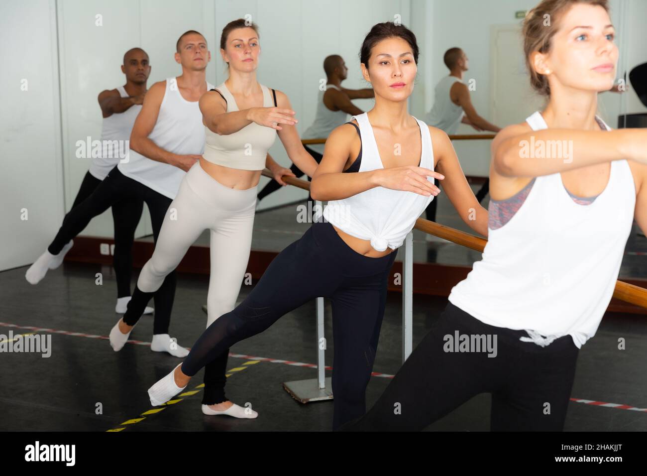 Group of multiethnic dancers standing with one hand on barre and ...
