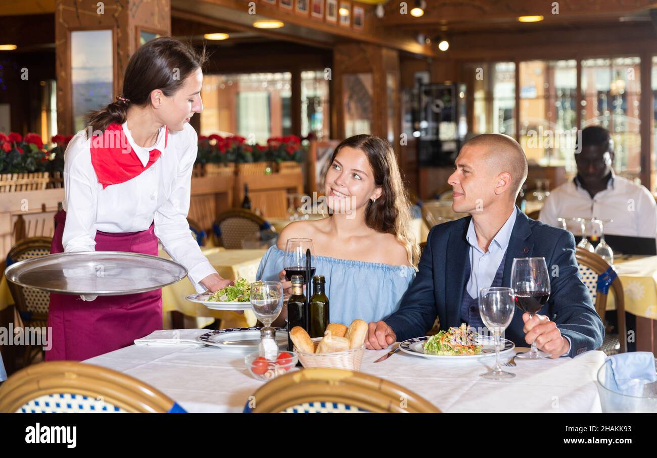 Diligent female waiter bringing order to visitors in restaurant Stock ...