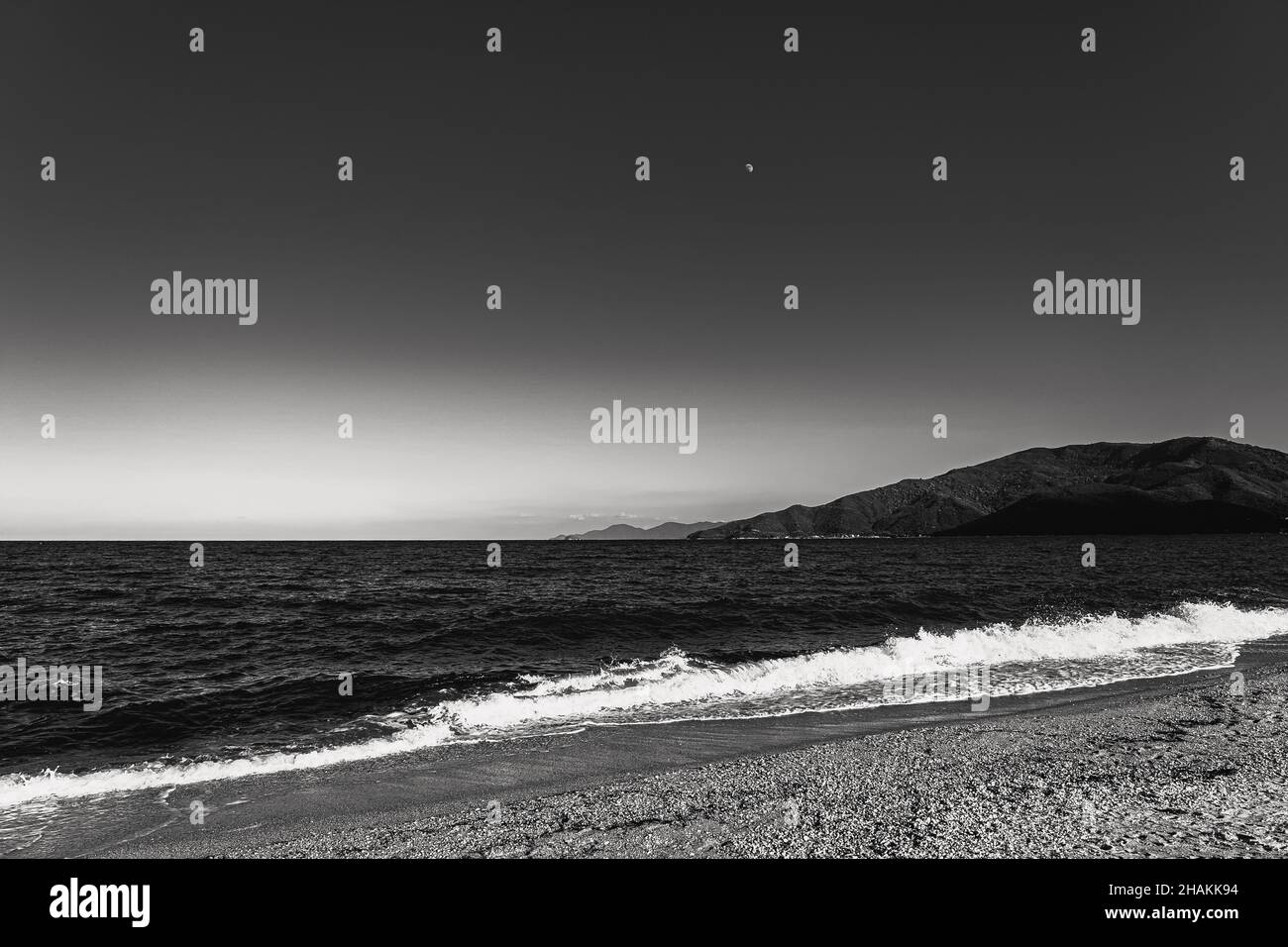 Grayscale shot of splashing sea waves against a sandy beach with a ...