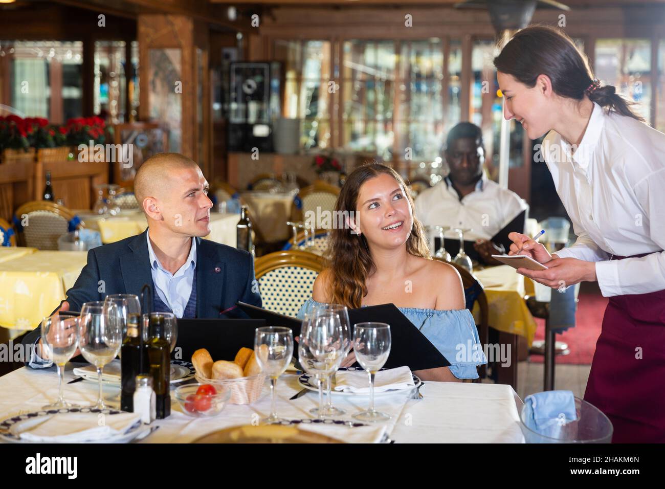 Young positive waitress taking table order from guests Stock Photo - Alamy