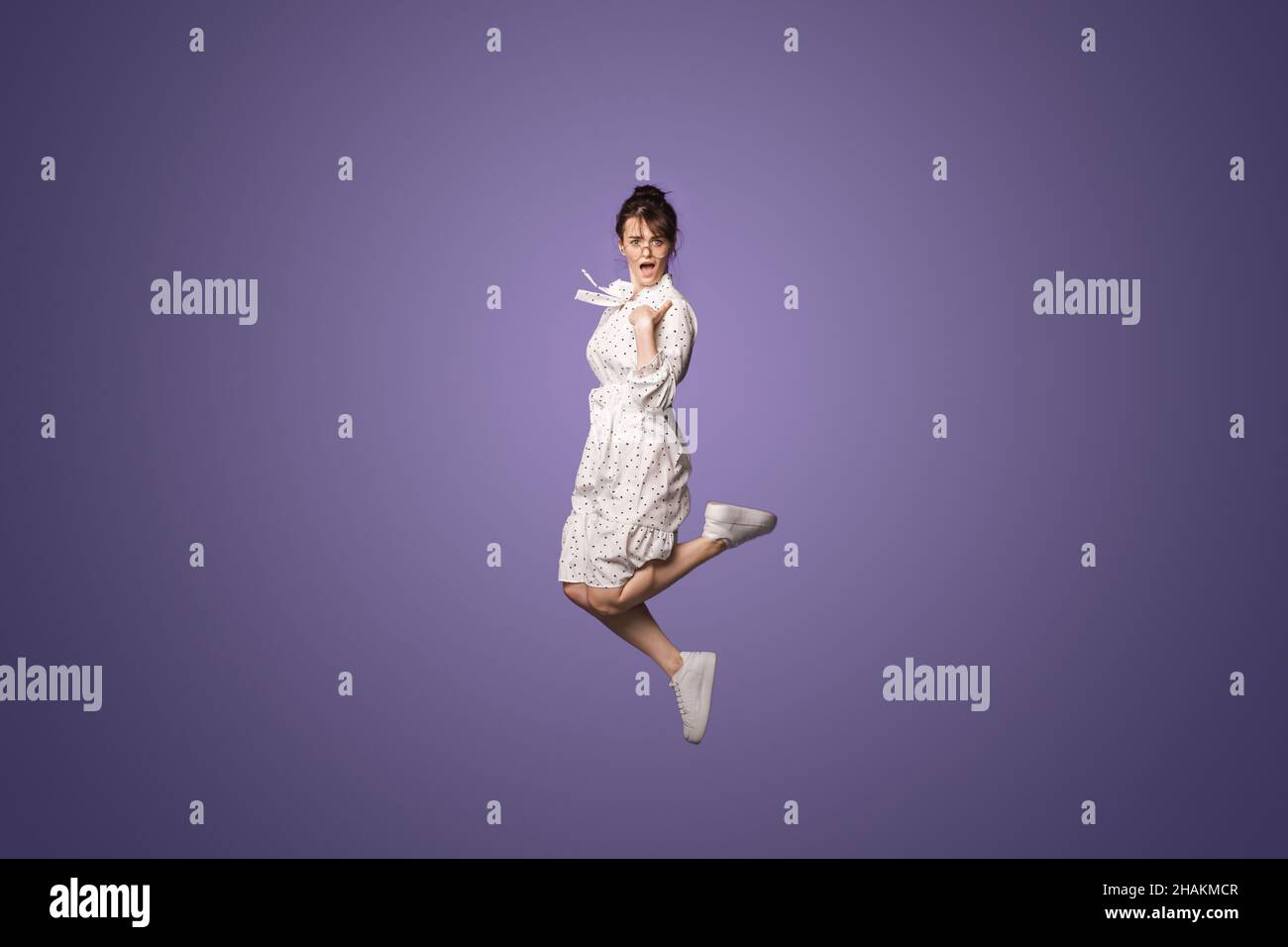 Full lenght of shocked young woman jumping over purple background wall ...