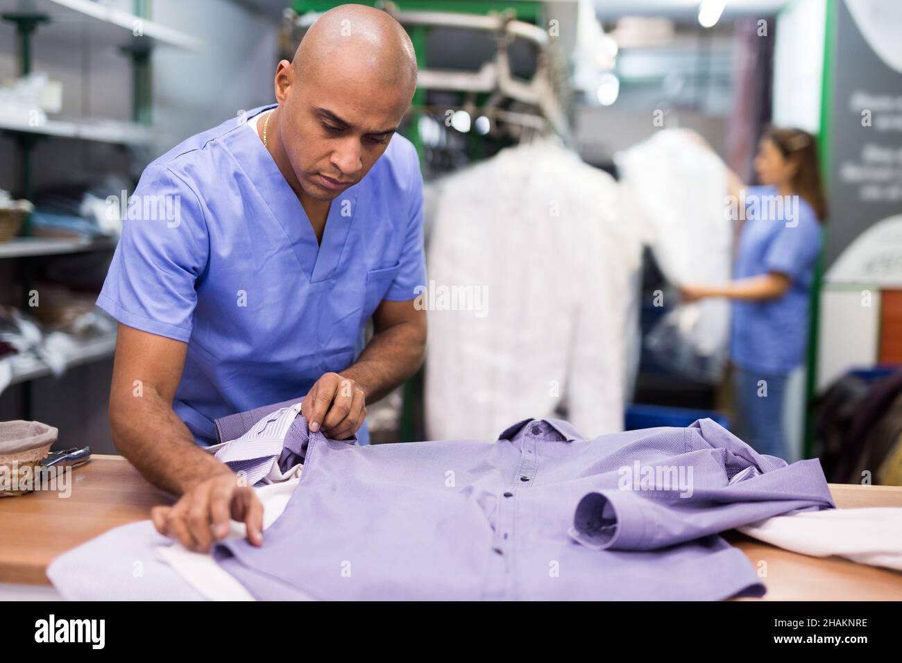 Confident man dry-cleaning worker checking clean clothes Stock Photo ...