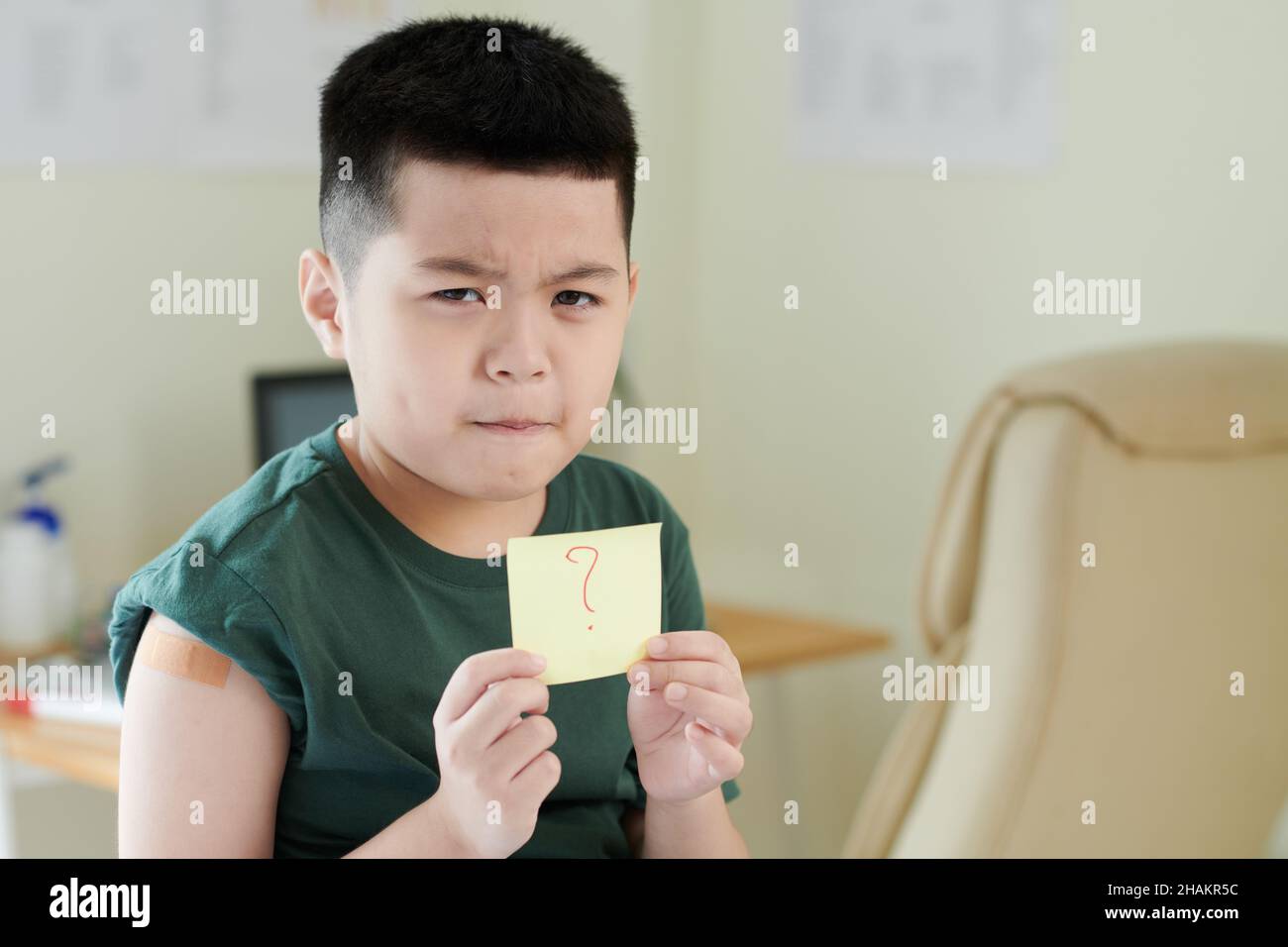 Frowning doubting little boy with adhesive plaster on shoulder showing ...