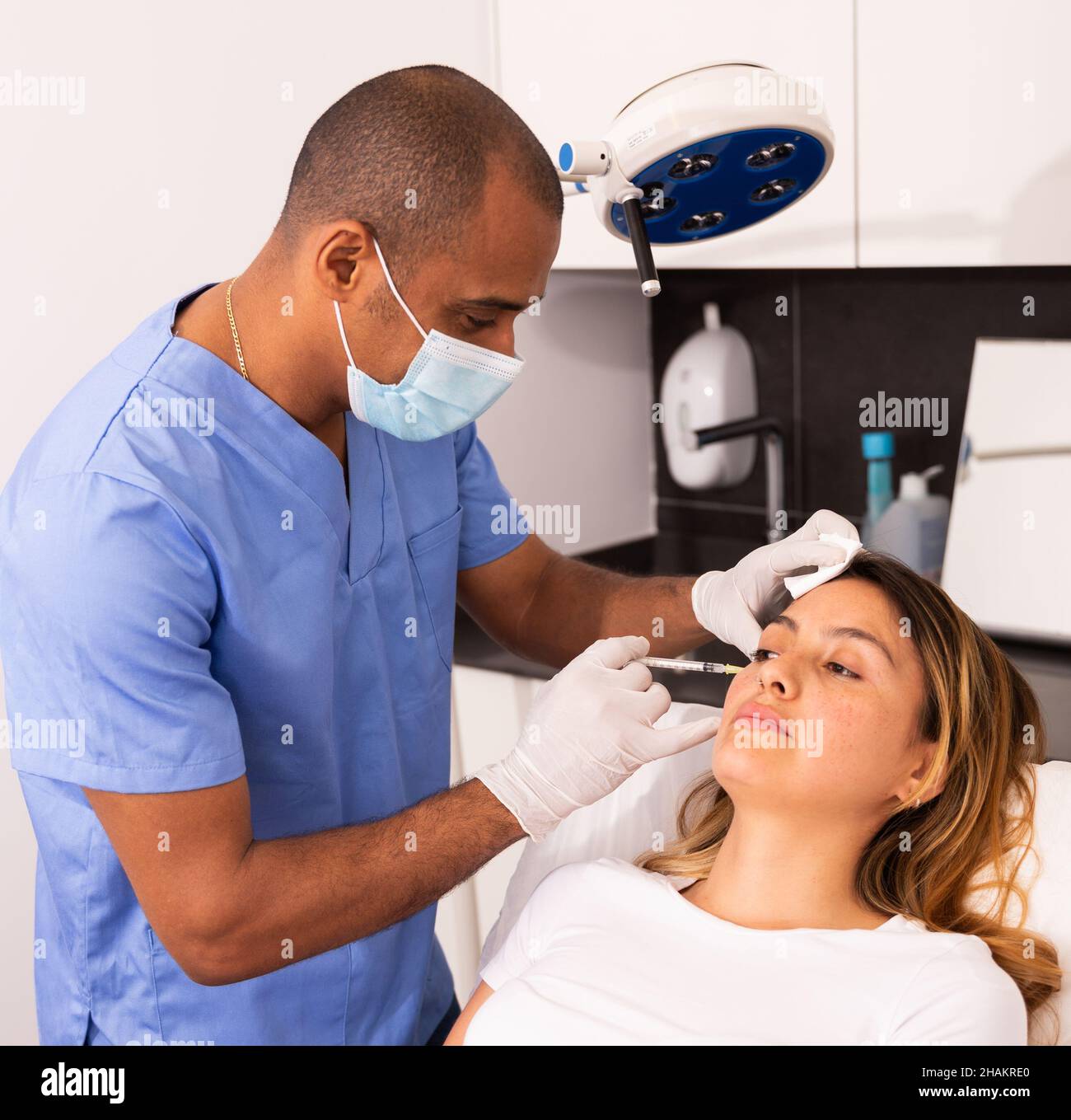 Male beautician performing face contouring injections to female Stock ...