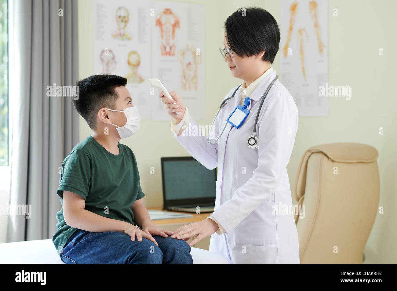 Smiling doctor checking body temperature of boy with non-contact ...