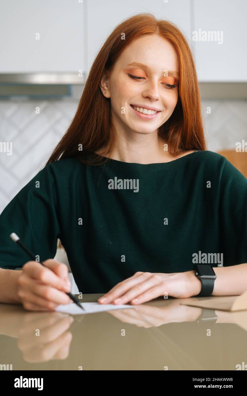 Vertical portrait of cheerful young woman writing handwritten letter ...