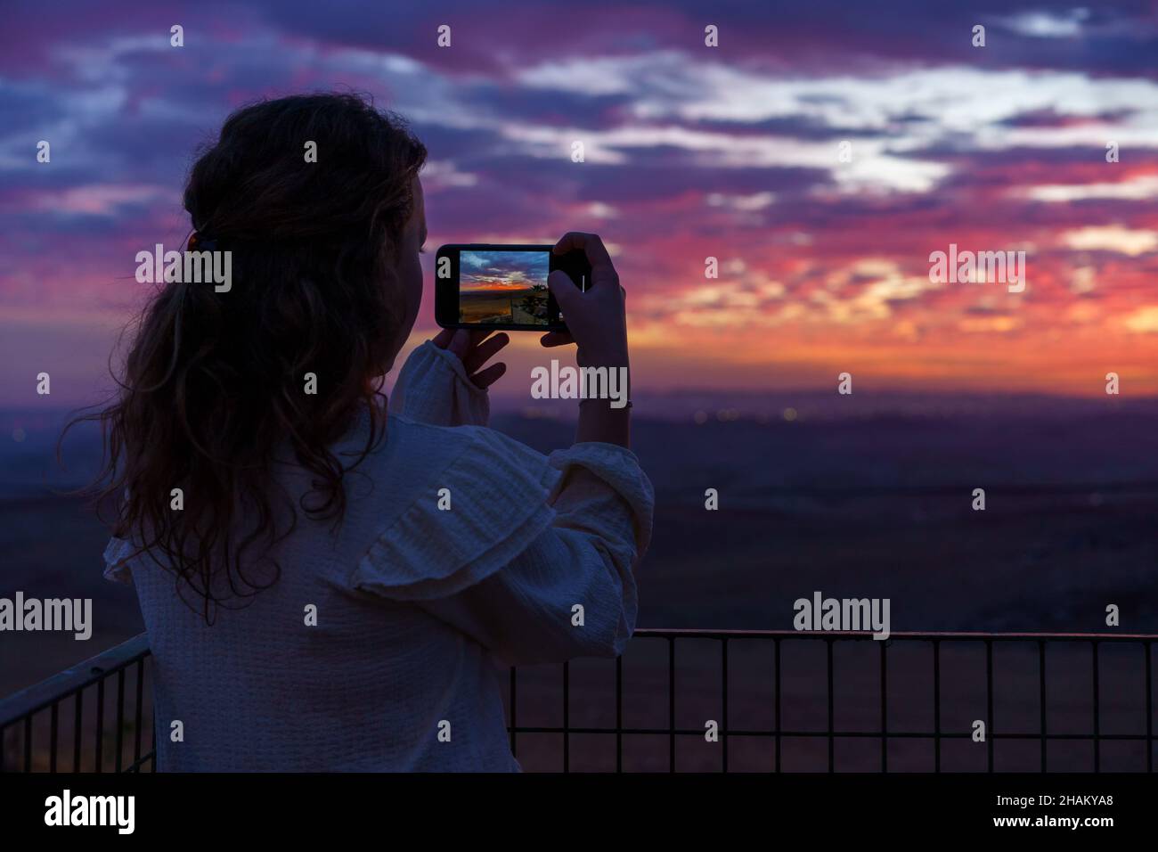 Back view beautiful little girl takes a picture of the amazing sunset ...