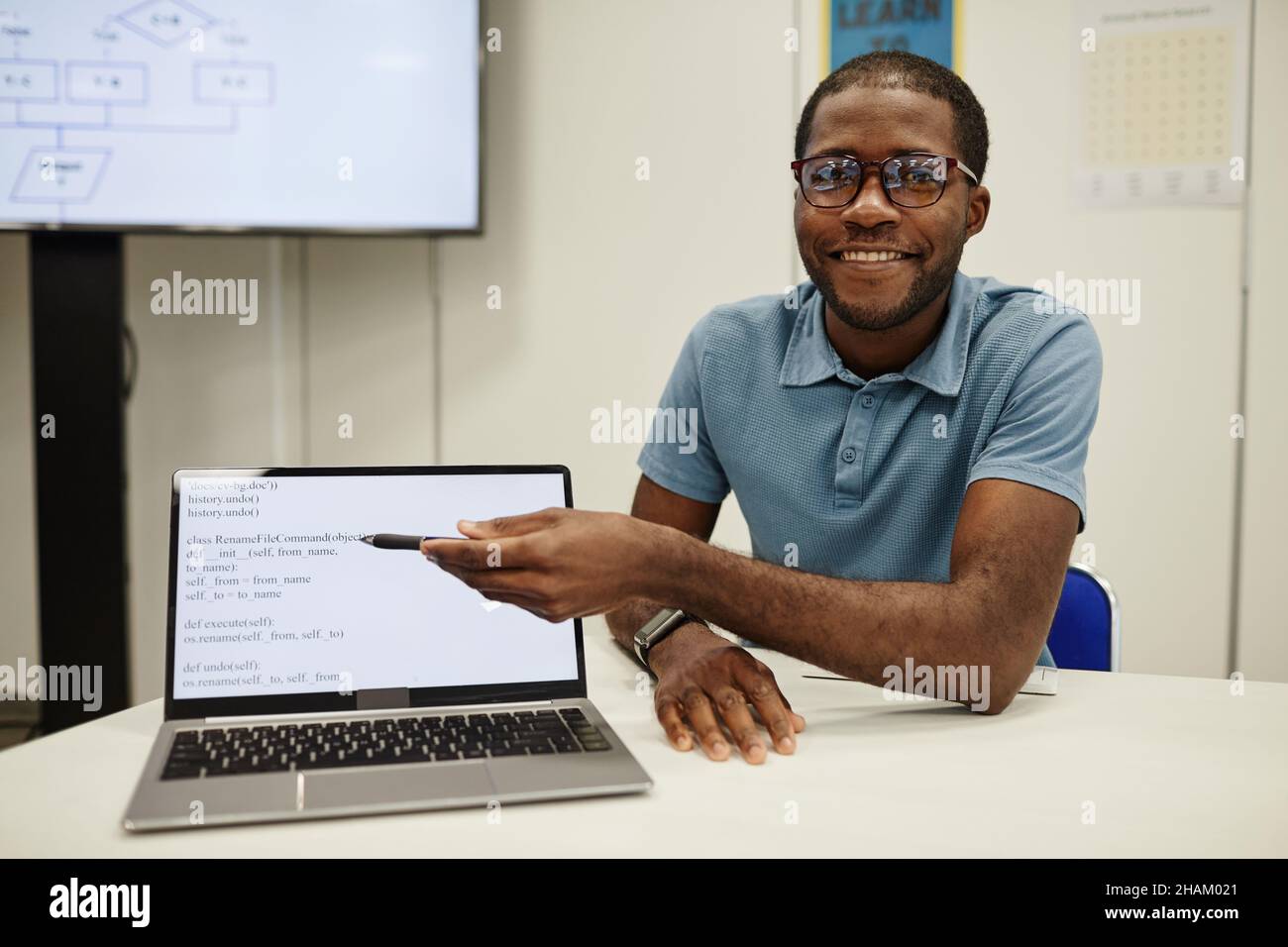 Portrait of young black teacher pointing at laptop screen in coding ...