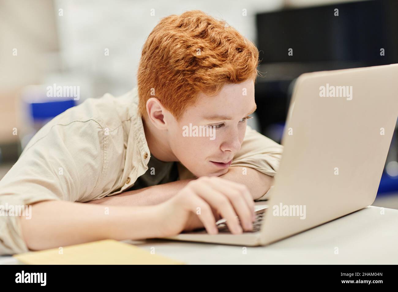 Portrait of red haired teenage boy laying head on desk while using ...
