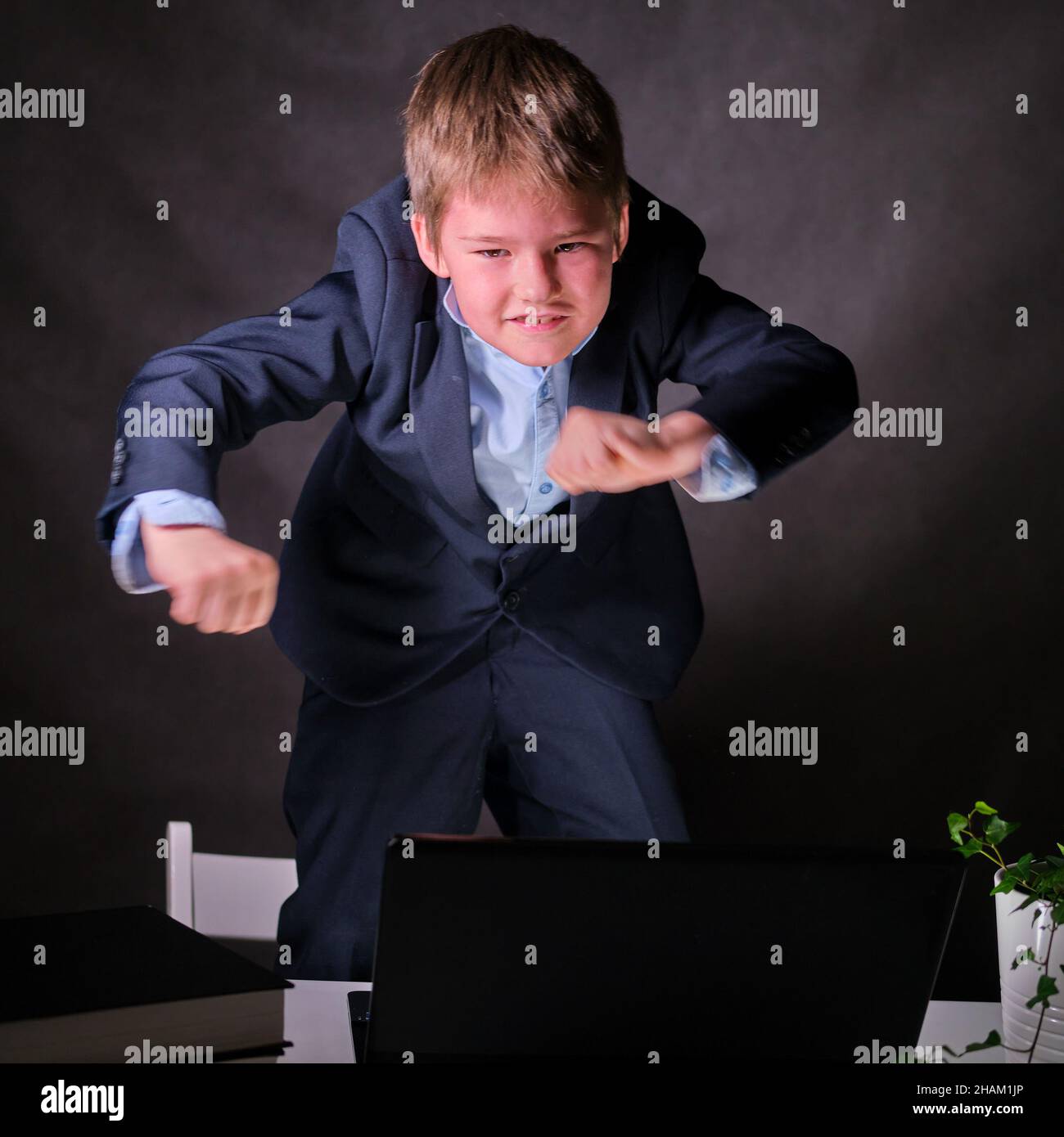 A boy dances at a table with a computer, copy space on a dark studio ...