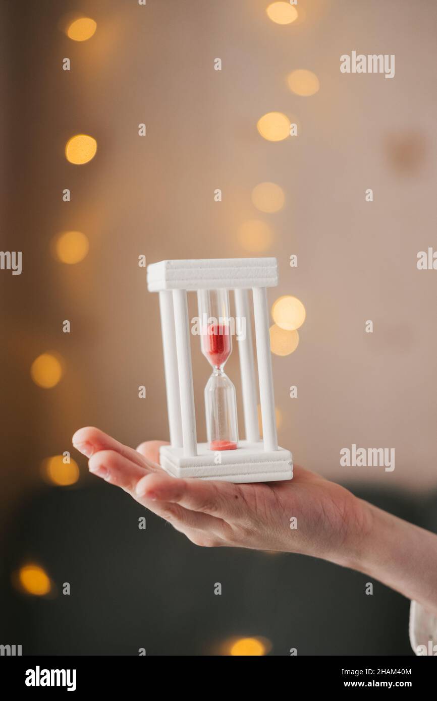 hands hold a white hourglass on the background of a Christmas garland ...