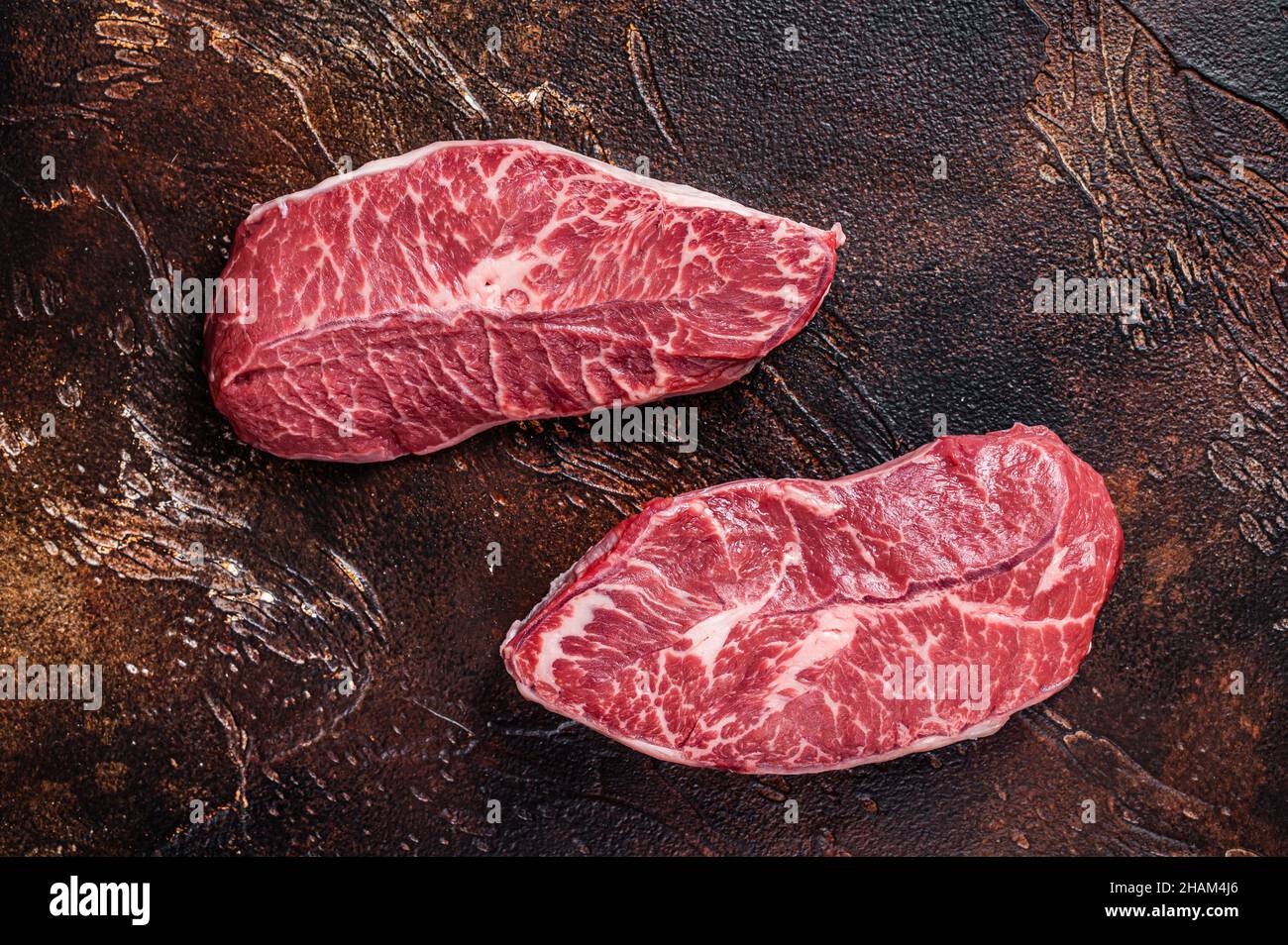 Raw Top Blade or flat iron beef meat steaks on a butcher table. Dark ...