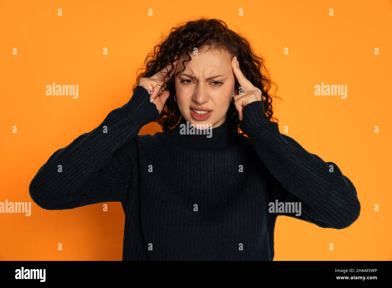 One emotive young girl in warm winter sweater isolated on orange studio ...