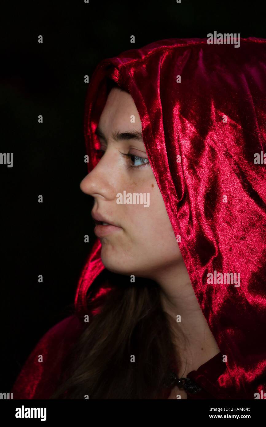 Side of face of teenage girl wearing a red cloak against a dark ...
