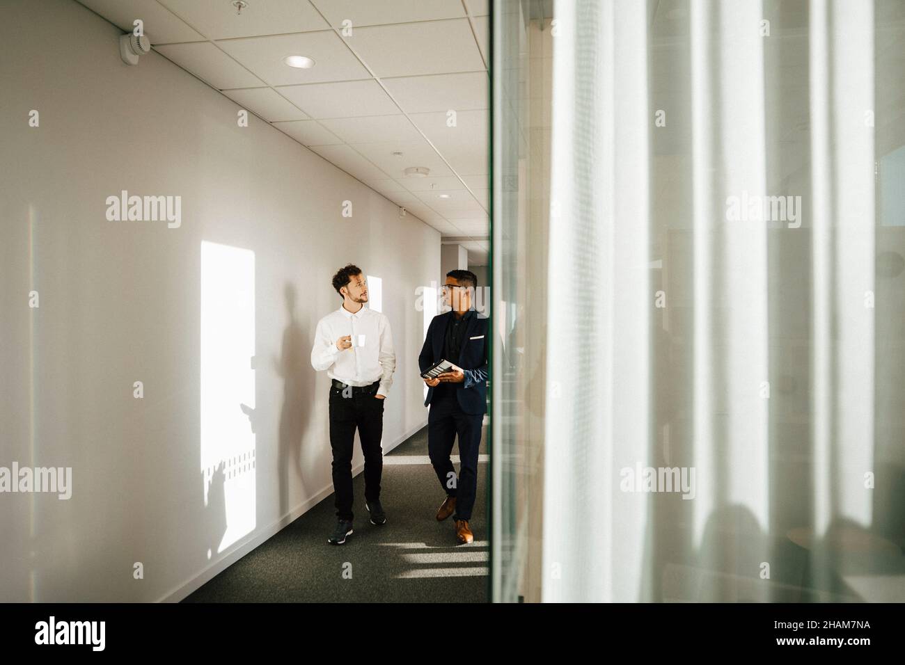 Coworkers talking at corridor Stock Photo - Alamy