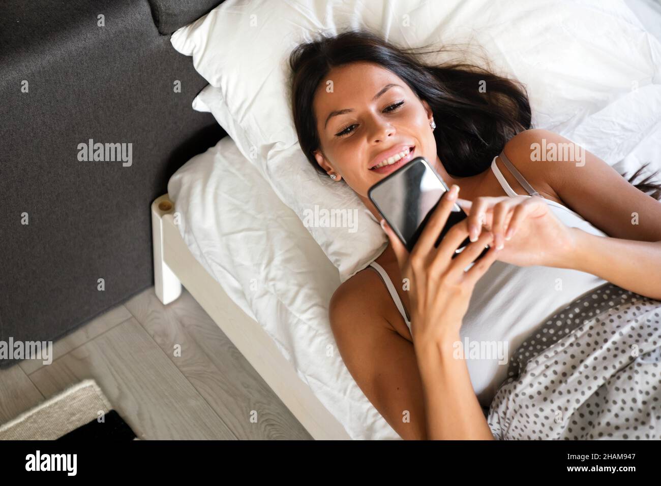 Technology, internet, communication and people concept. Happy woman texting on smartphone in bed ...