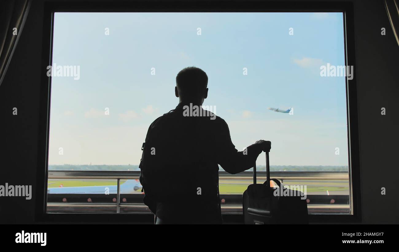 A young man with baggage watches the airplane take off from the window ...