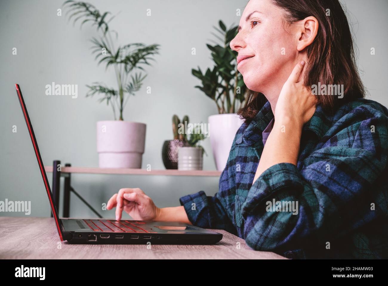 A woman suffering form neck stiffness while sitting at her laptop and ...