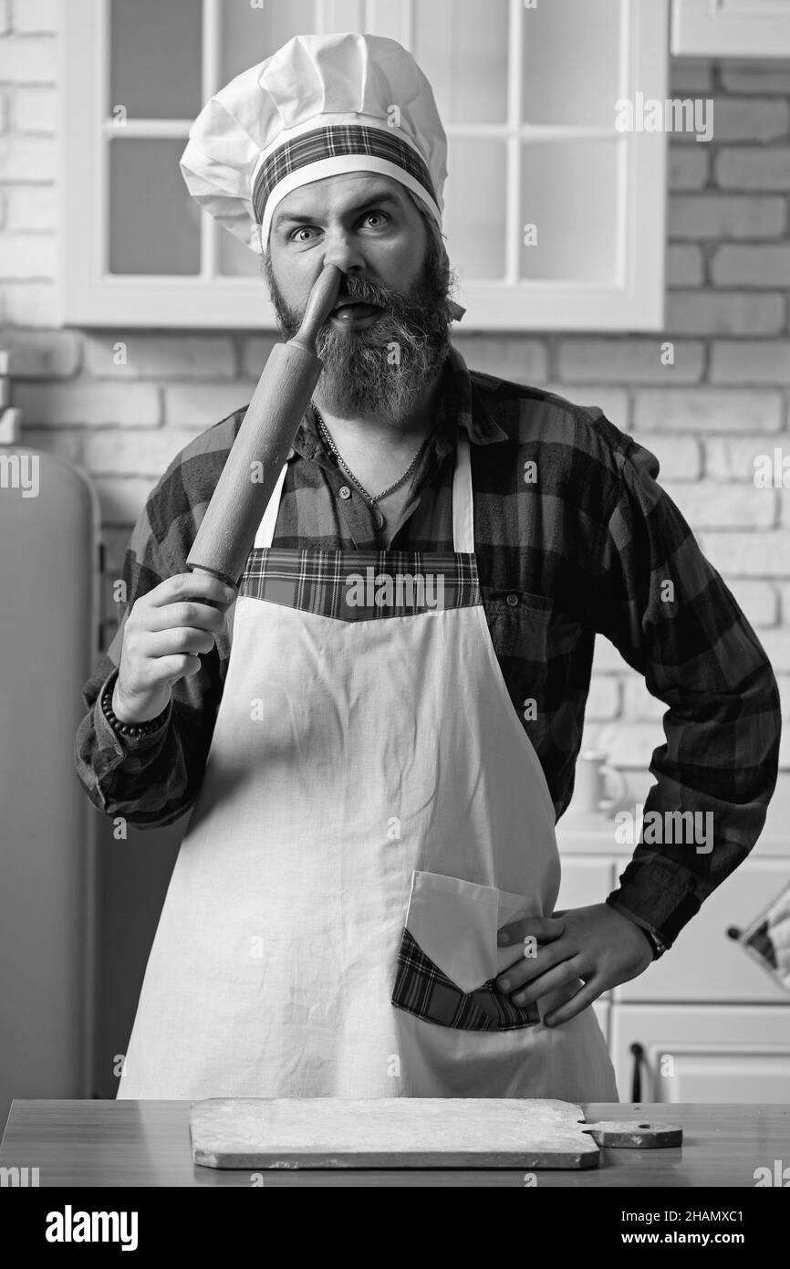 Bearded chef sticks a rolling pin in his nose. Crazy chef in a white ...