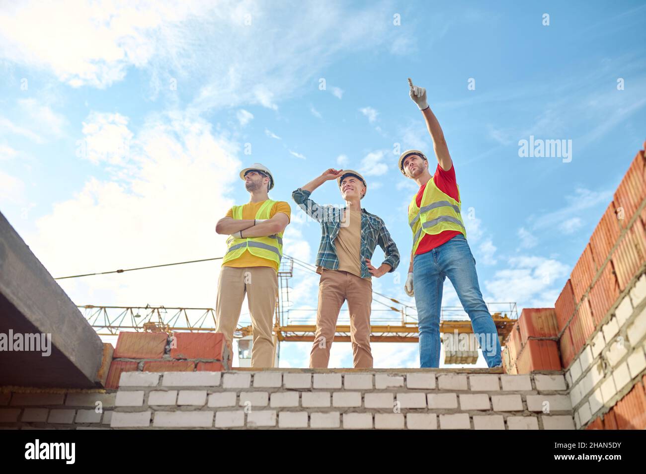 Men standing on brick wall of building under construction Stock Photo ...