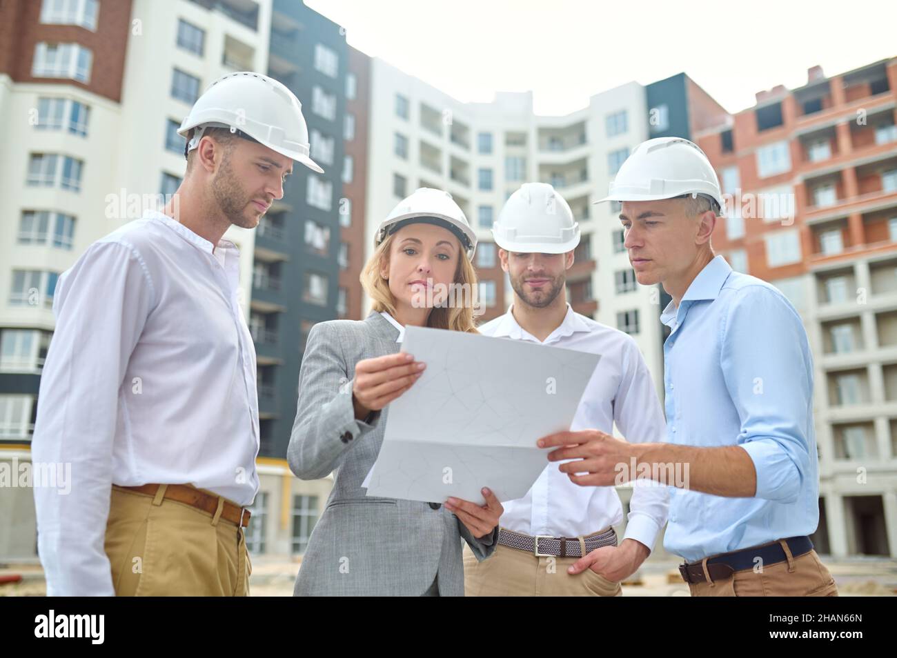 Woman and men looking at drawing at construction site Stock Photo - Alamy