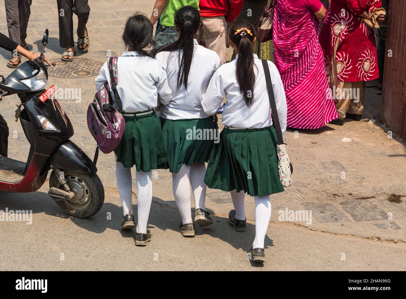 Three adolescent Nepali girls in school uniforms walk arm in arm in ...