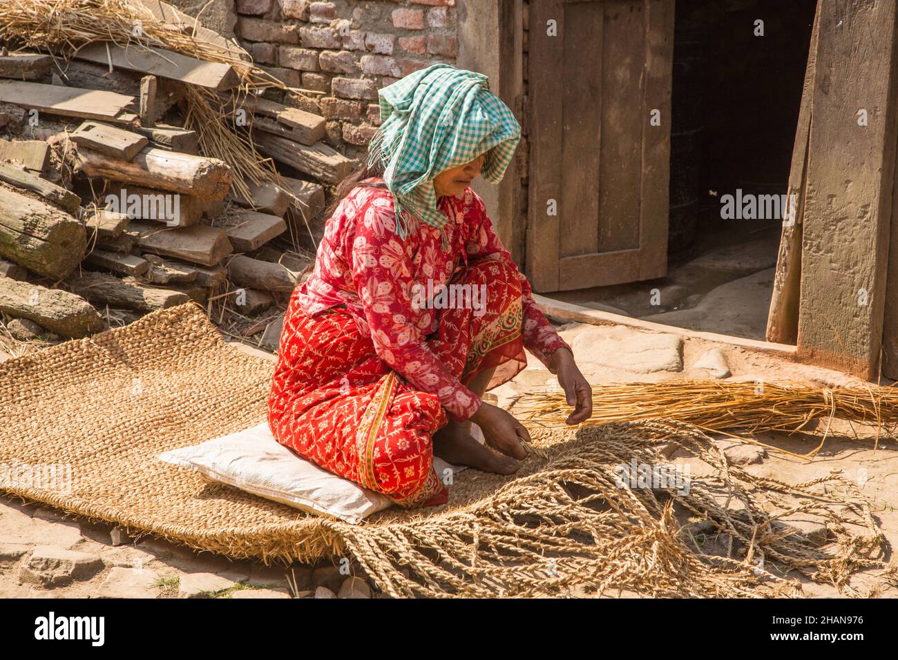 A Nepali woman weaves a jute mat in front of her house in the medieval ...