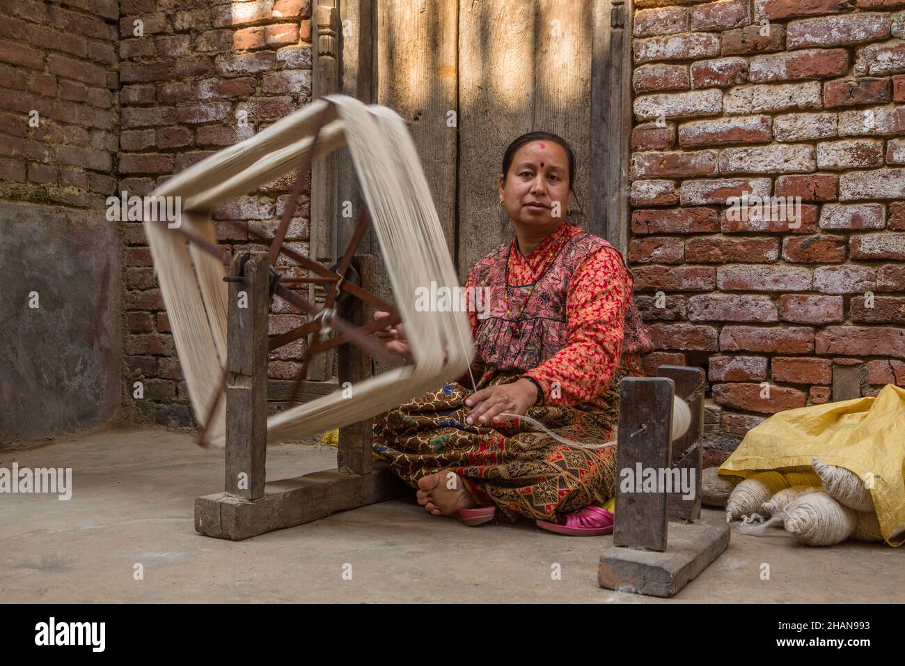 A Nepali woman spins wool thread with a hand-cranked spinning wheel in ...