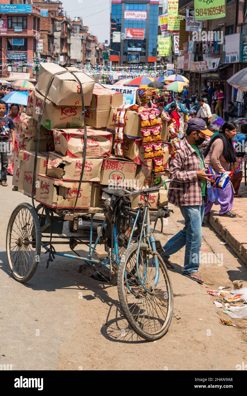 A Nepali man carrying boxes of snack chips on a tricycle cart in Patan ...