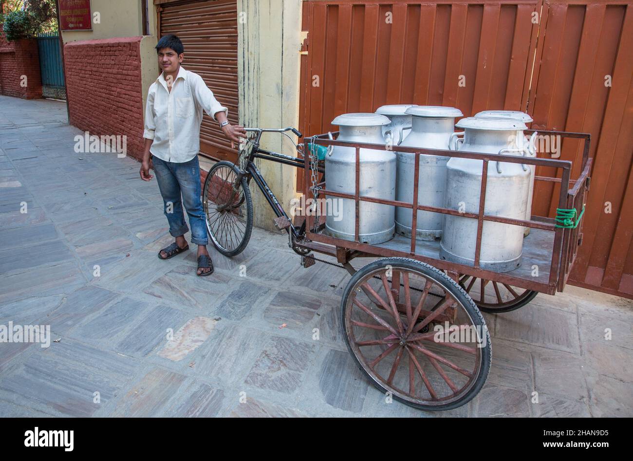 A young Nepali man carrying large metal milk jugs in a tricycle cart in ...
