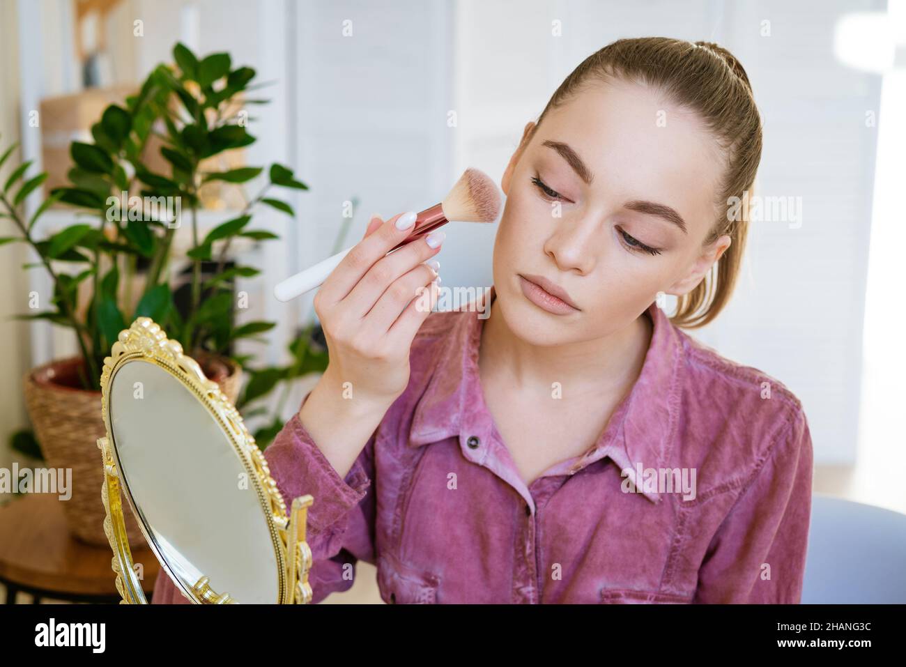 Beautiful young woman makes blush on her face using makeup brush while ...
