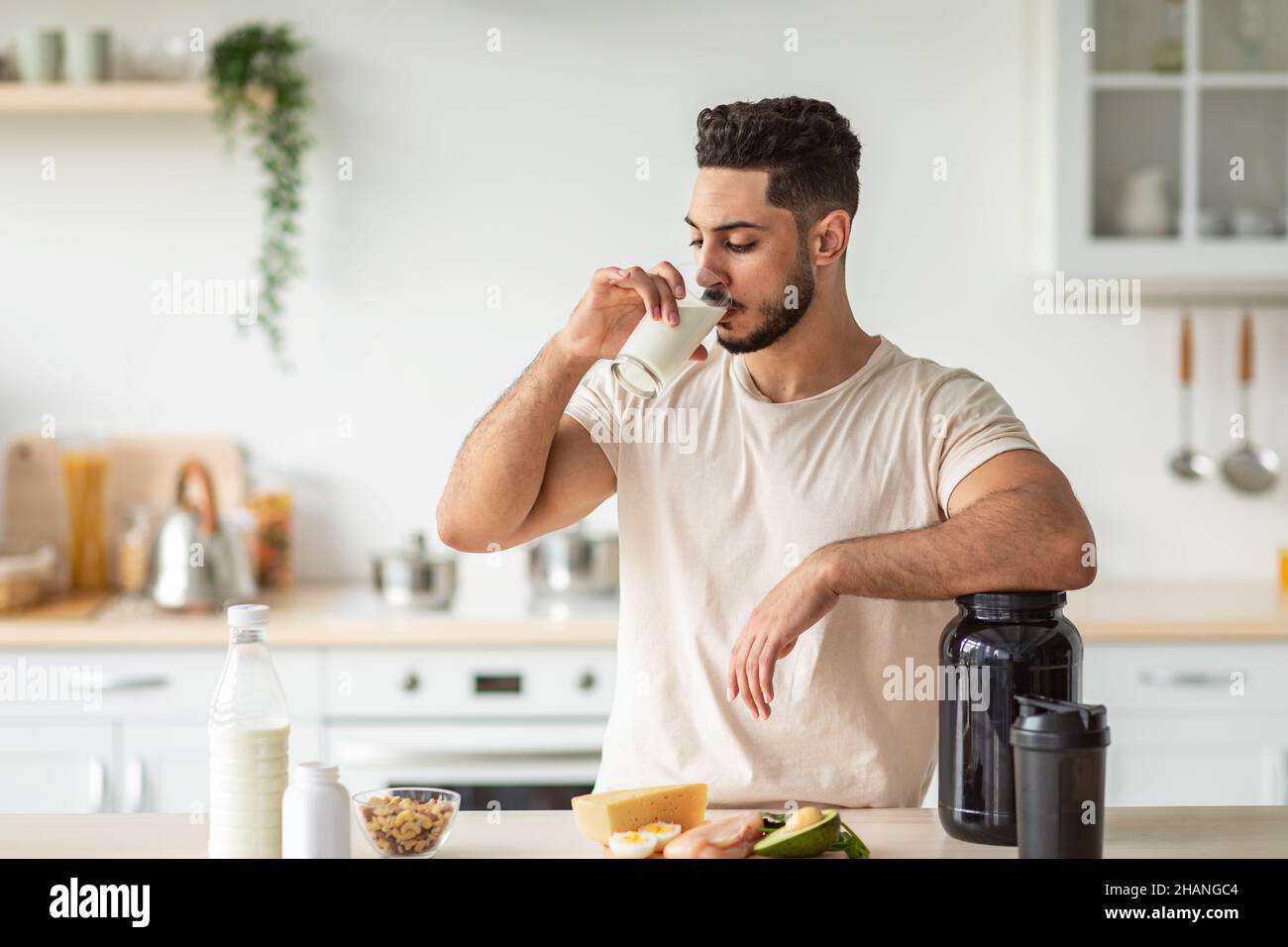 Athletic young Arab man drinking protein shake or milk, standing near ...