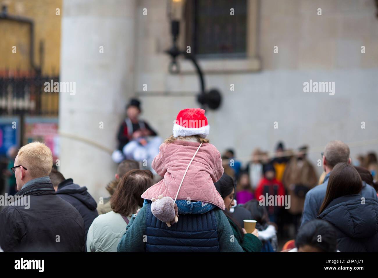 A child wearing a Santa Claus hat watches a performer as people gather ...