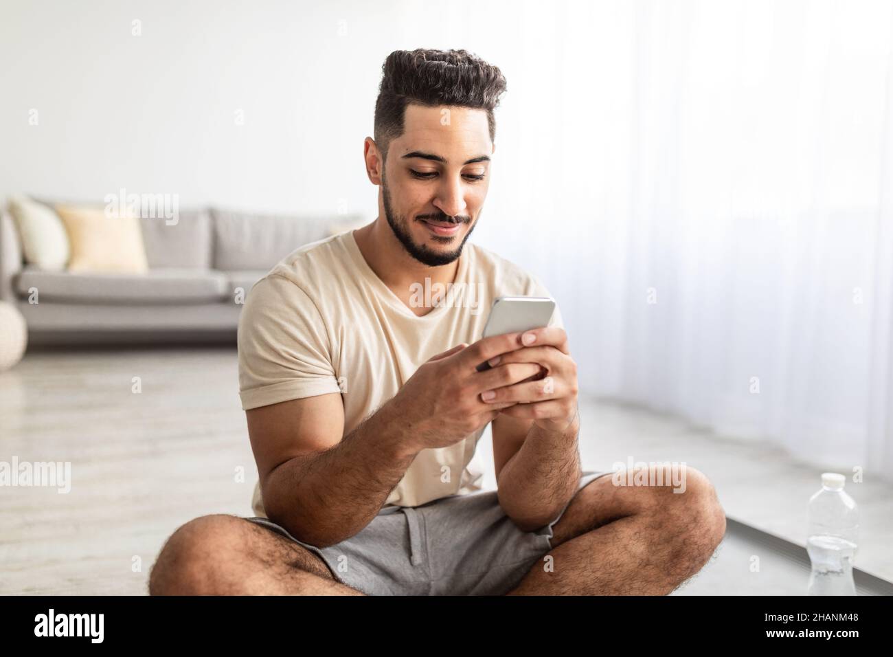 Strong young Arab man using cellphone at home gym, communicating to ...