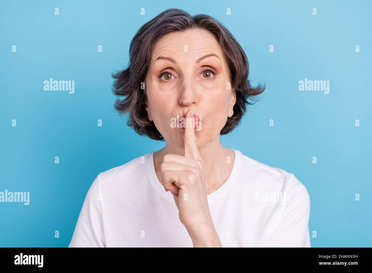 Portrait of attractive grey-haired woman showing shh sign isolated over ...