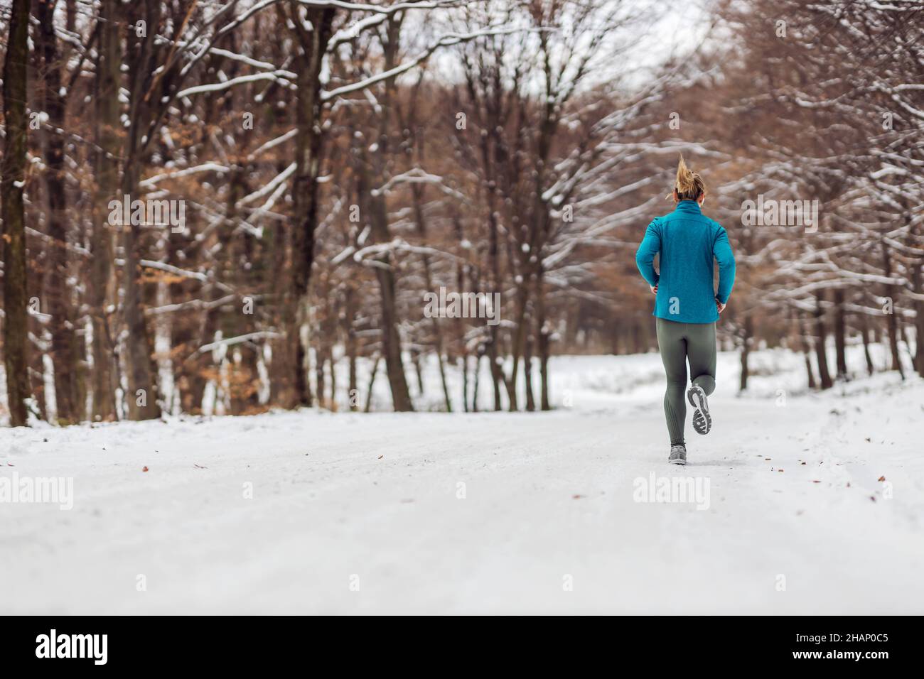 Rear view of sportswoman jogging in nature on a snowy weather. Cold ...